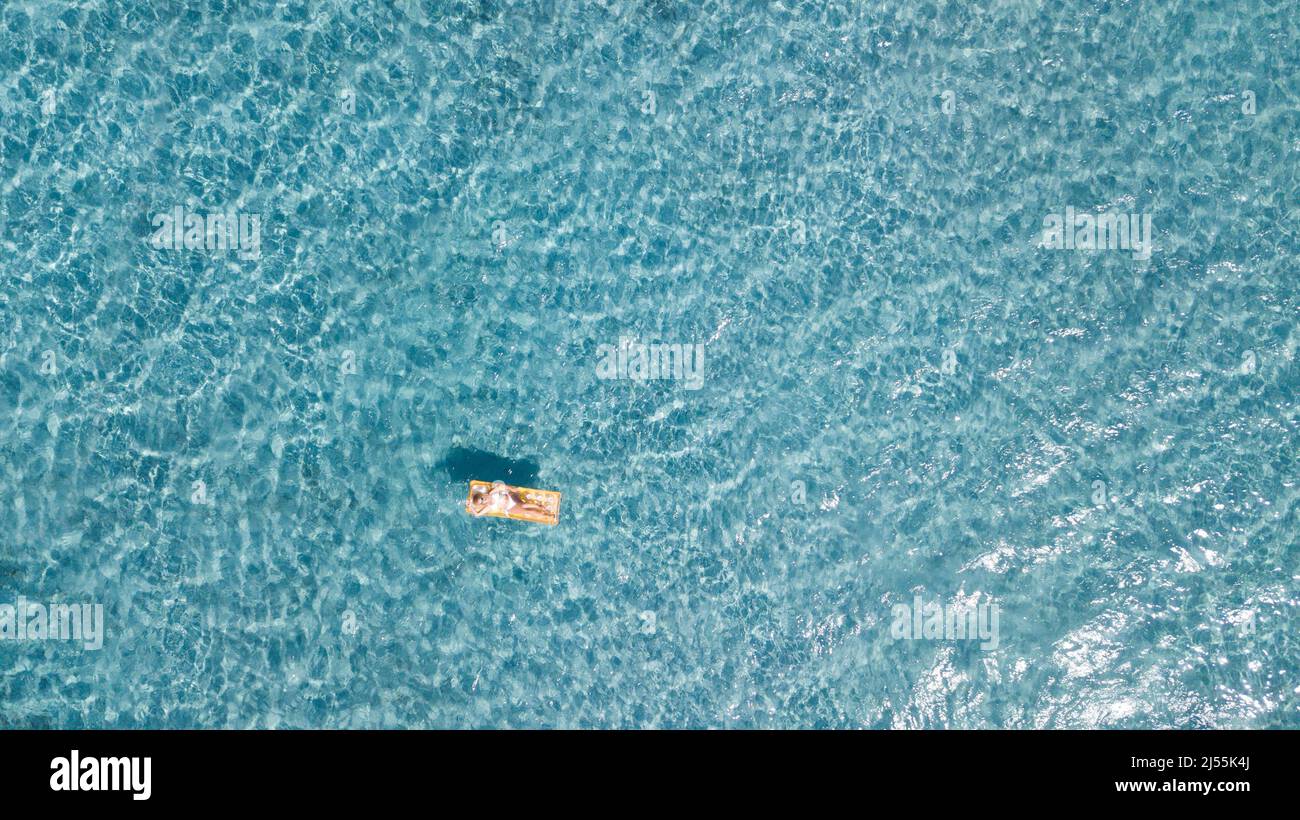 Woman floating on lilo inflatable mattress over blue transparent water ...