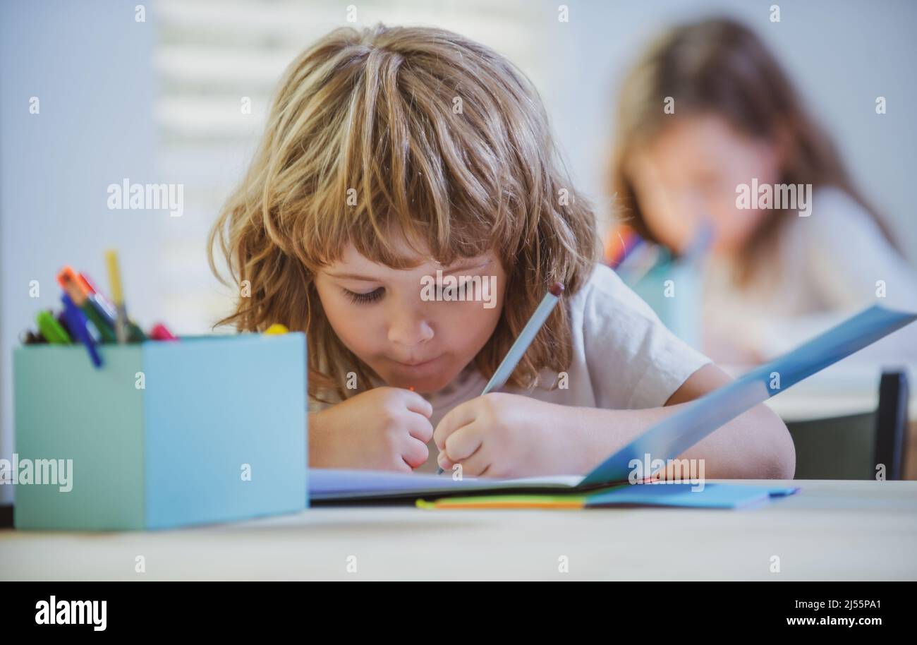 School kid writing something in copybook and sitting at table in ...