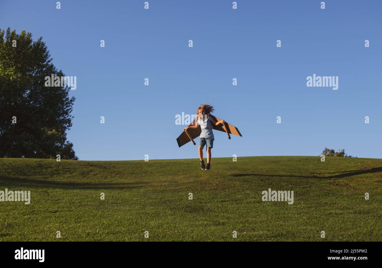Child running jumping and flying with toy plane wings on grass in park ...