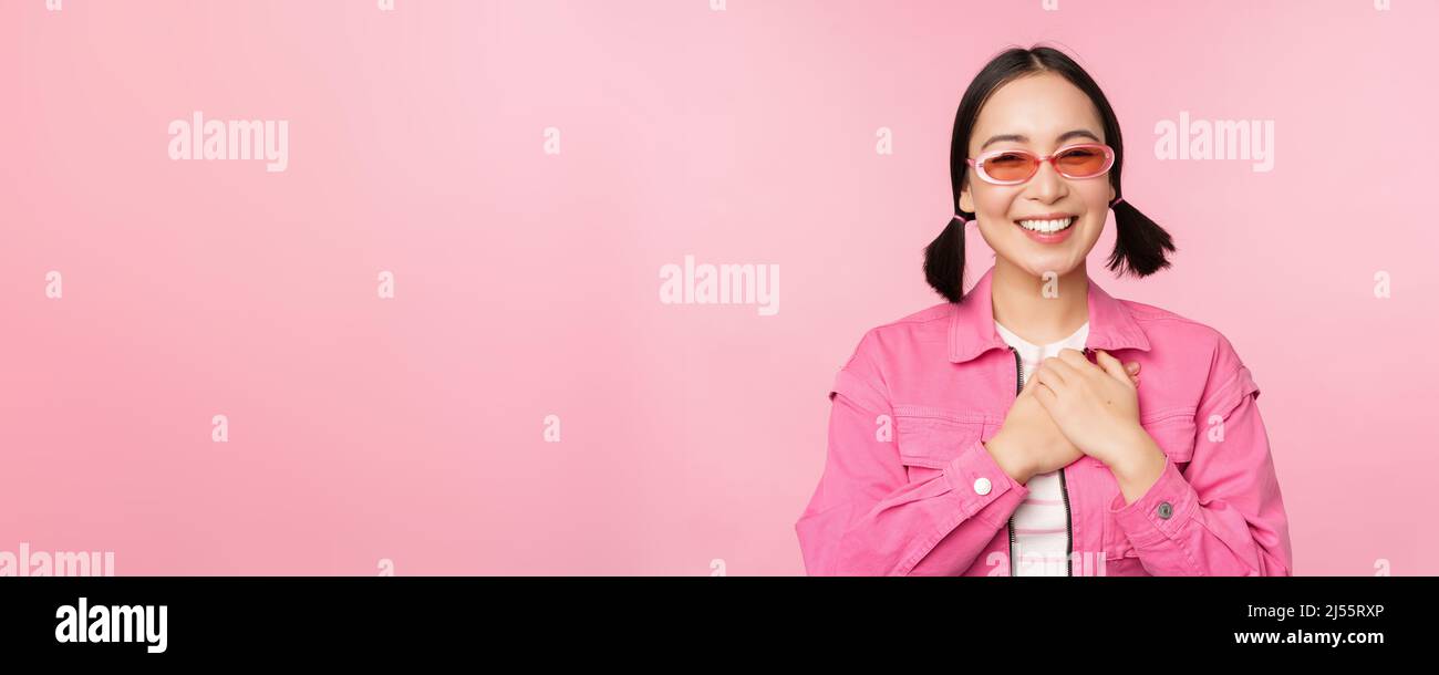 Smiling young asian woman in sunglasses looking thankful, holding hands ...