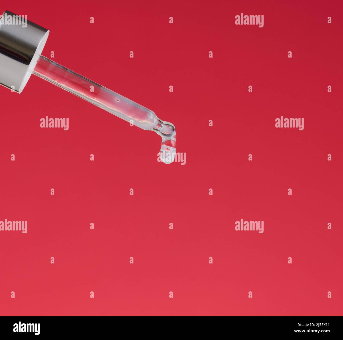 glass pipette with dripping transparent liquid on a red background ...