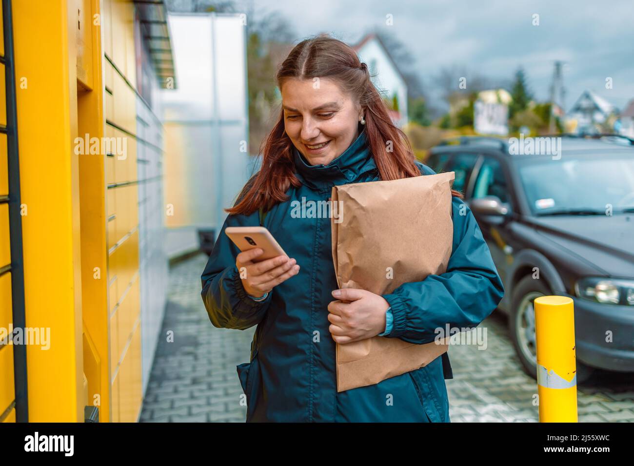 Young caucasian woman getting parcel from cell of automatic post ...