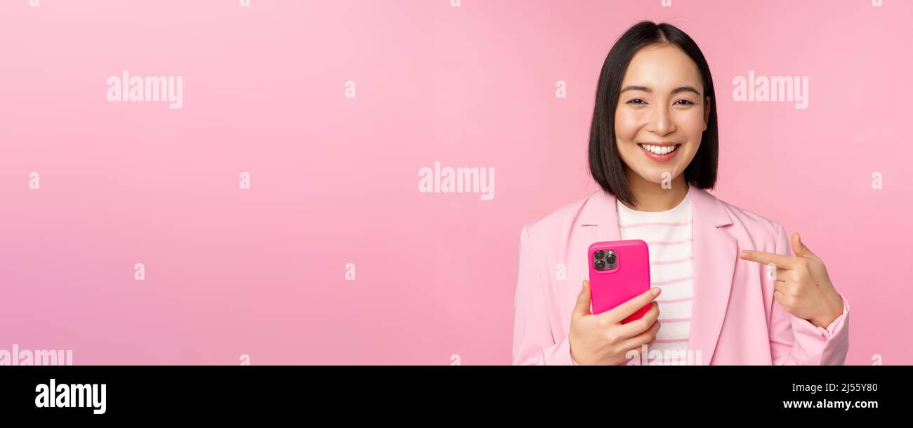 Portrait of smiling asian businesswoman pointing at her mobile phone ...