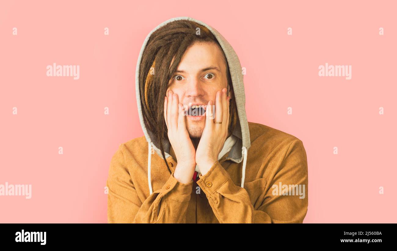 Young shocked man leaning hands against cheeks and opening mouth ...