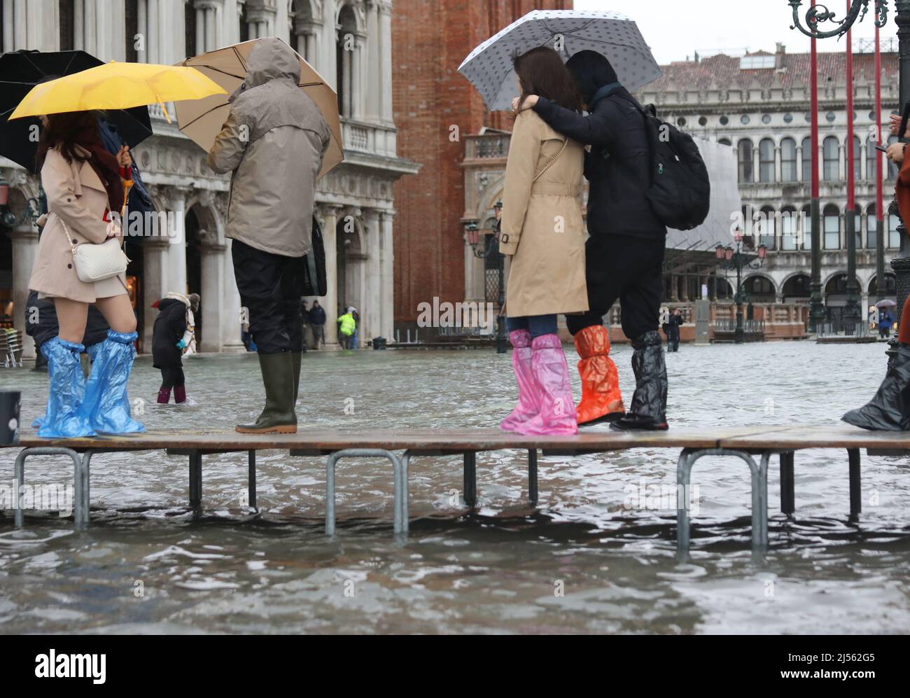 venice at high tide and people walking over the elevated walkway with ...