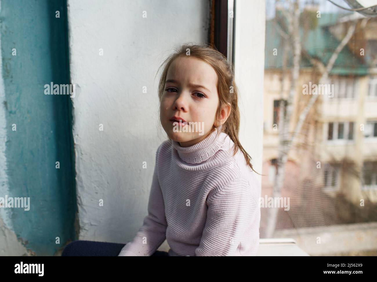 a sad little girl is sitting by the window with tears in her eyes Stock ...