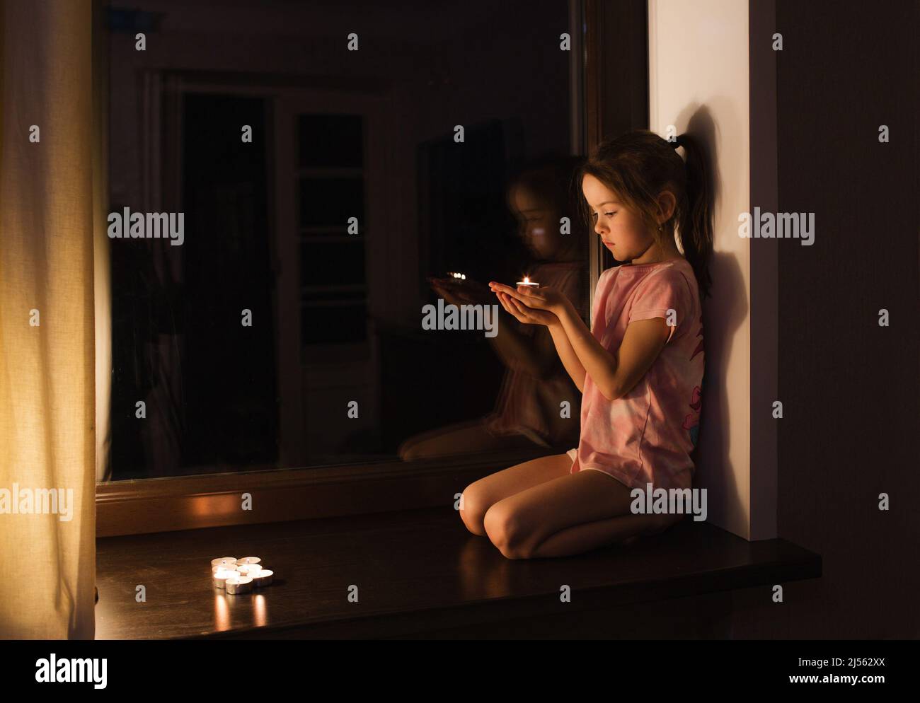 The silhouette of a small lonely girl holding a burning candle in the ...