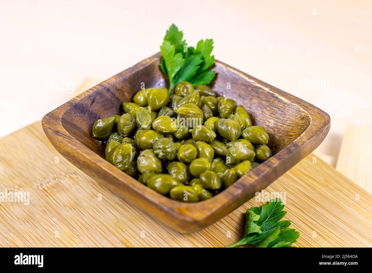Small green pickled capers fruit in a wooden bowl on light background ...