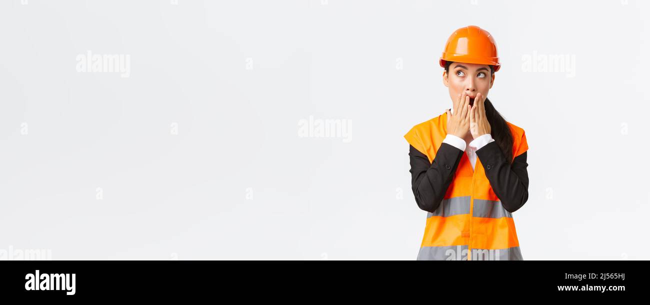 Shocked and concerned asian female engineer, architect in safety helmet ...