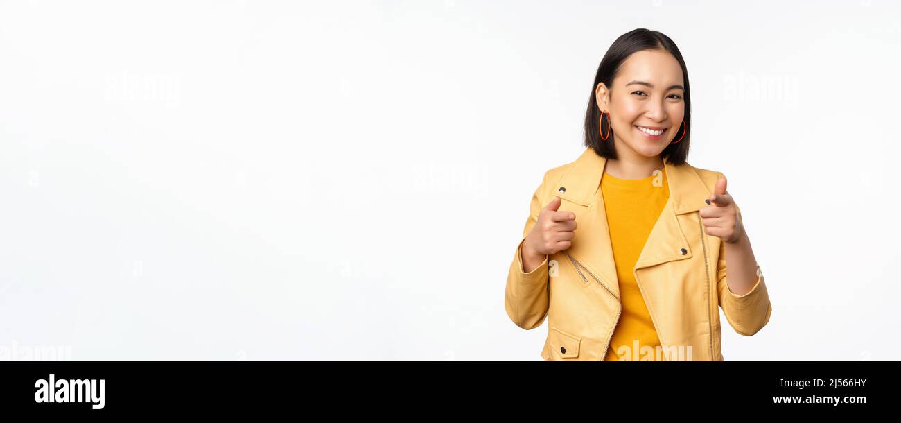 Hey you. Happy smiling asian woman pointing fingers at camera, choosing ...