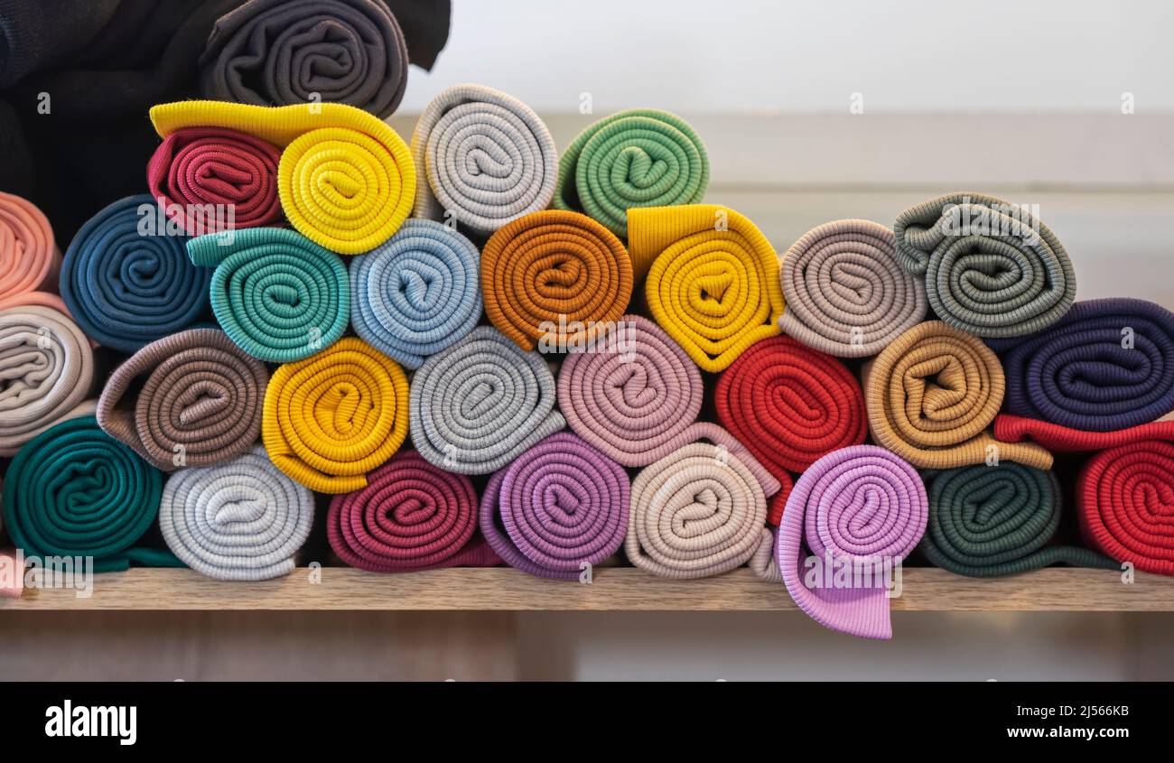 Multi-colored knitted fabrics rolled up in rolls lying on shelf of ...