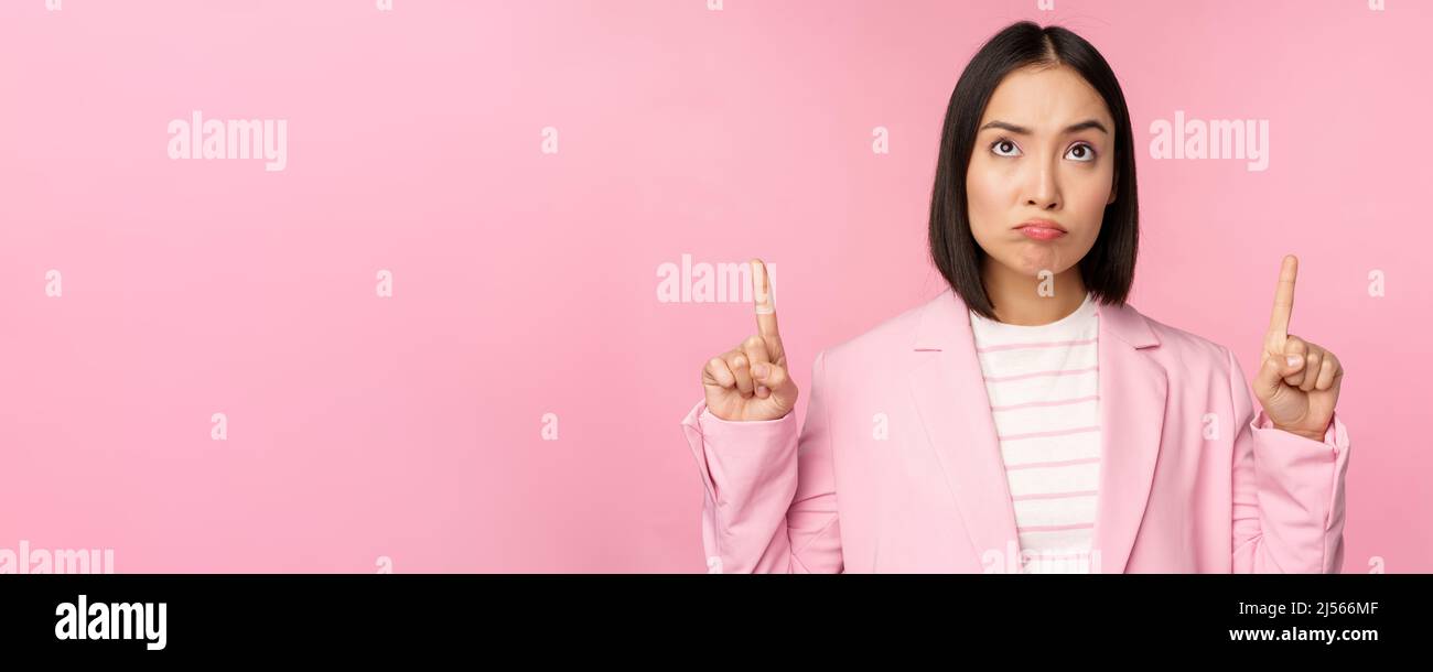 Upset asian corporate woman in office suit, pointing and looking up ...