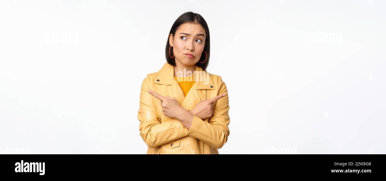 Image of indecisive asian girl, pointing fingers sideways, pointing ...