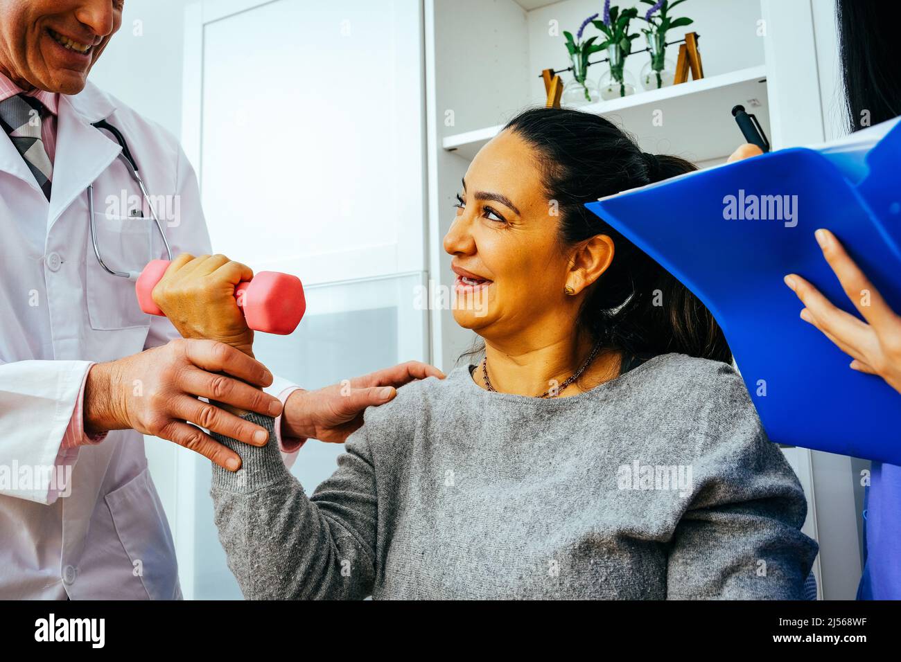 Close up doctor physiotherapist and nurse helping happy patient lift ...