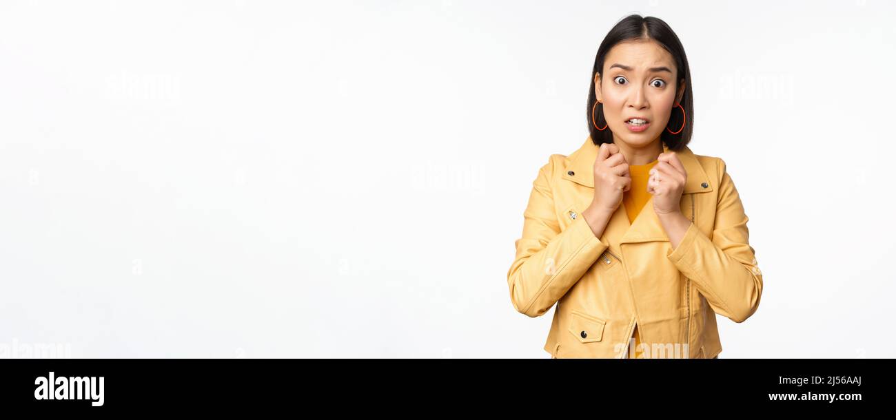 Image of scared asian woman looking insecure and worried at camera ...