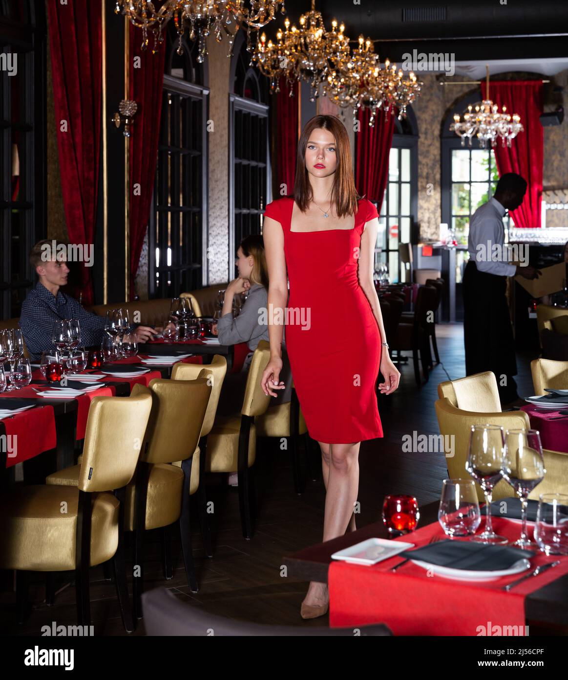 Attractive young woman in red dress walks through hall of a fashionable ...