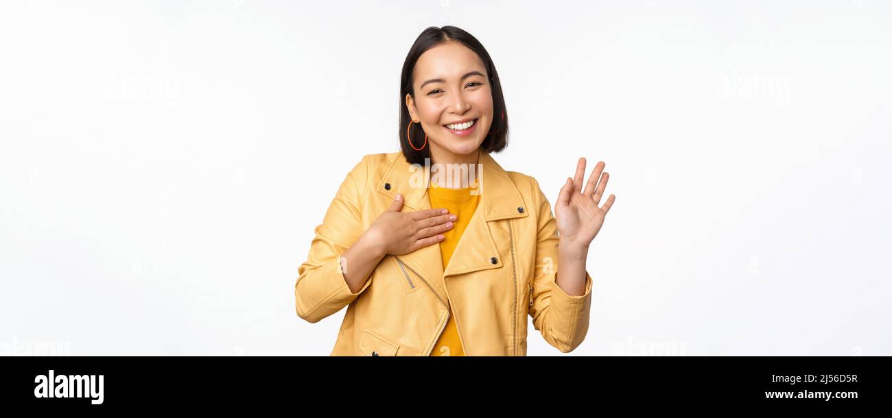 Image of friendly asian girl in stylish yellow coat, raising arm ...