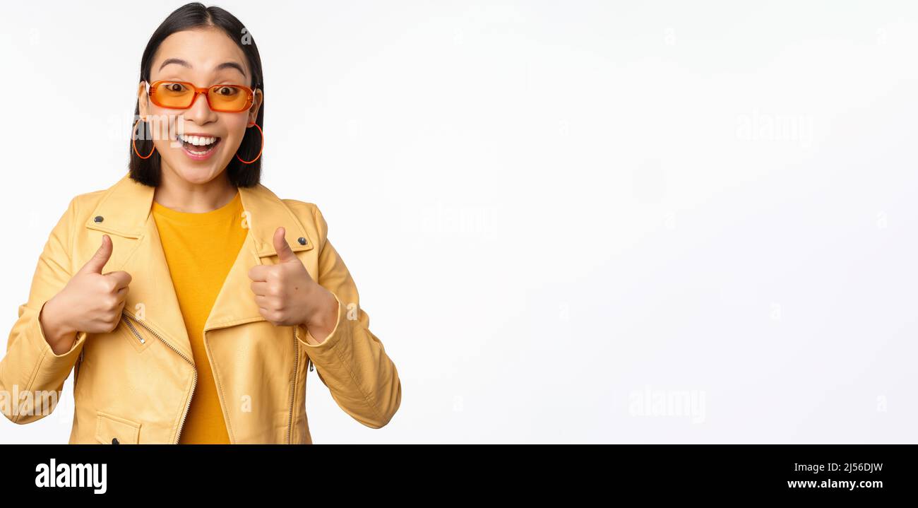 Enthusiastic asian girl smiles, shows thumbs up and looks happy, saying ...