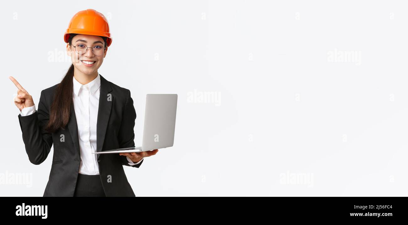 Smiling professional asian female engineer or architect at construction, wearing safety helmet ...