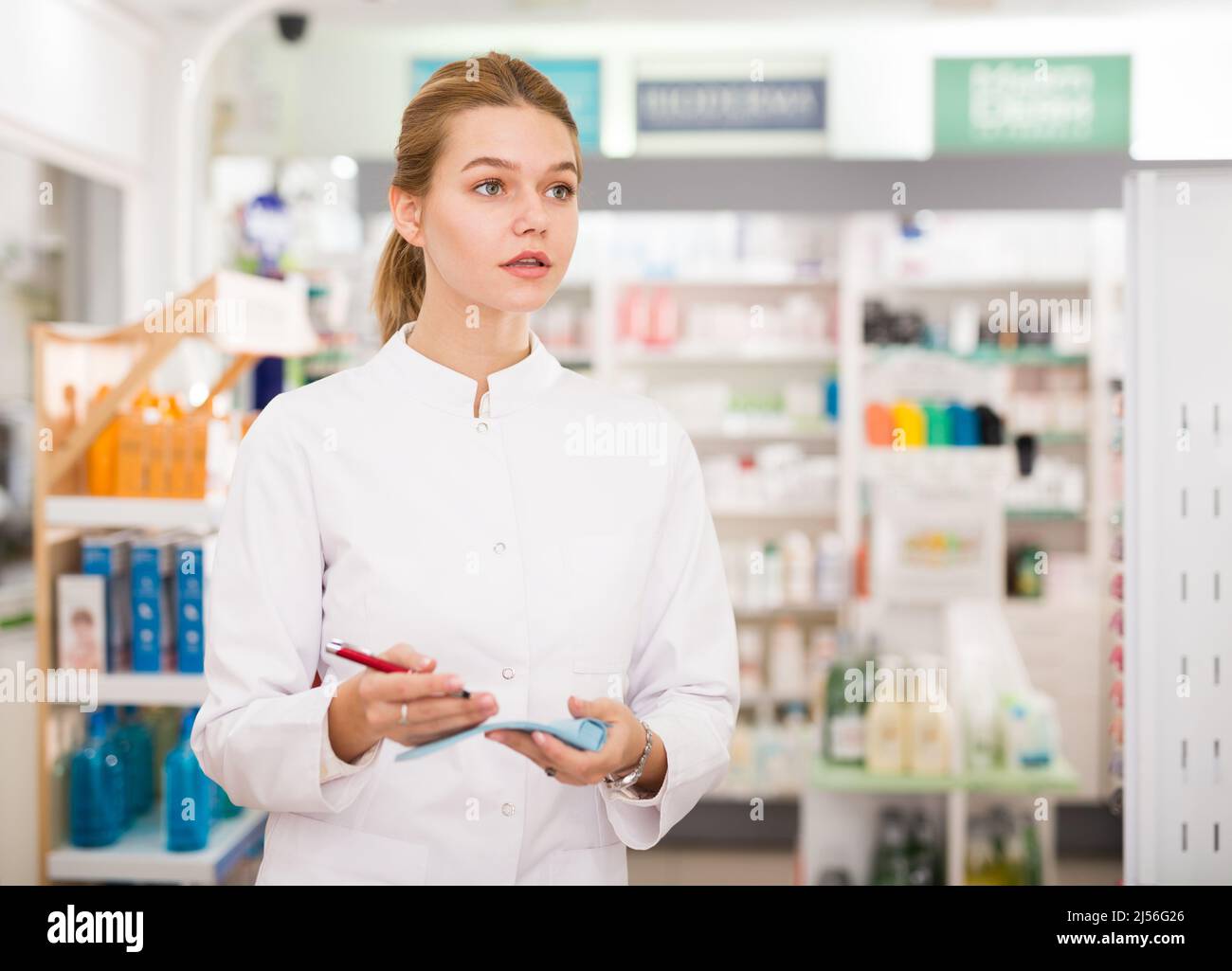 Diligent friendly smiling female pharmacist noting assortment of drugs ...