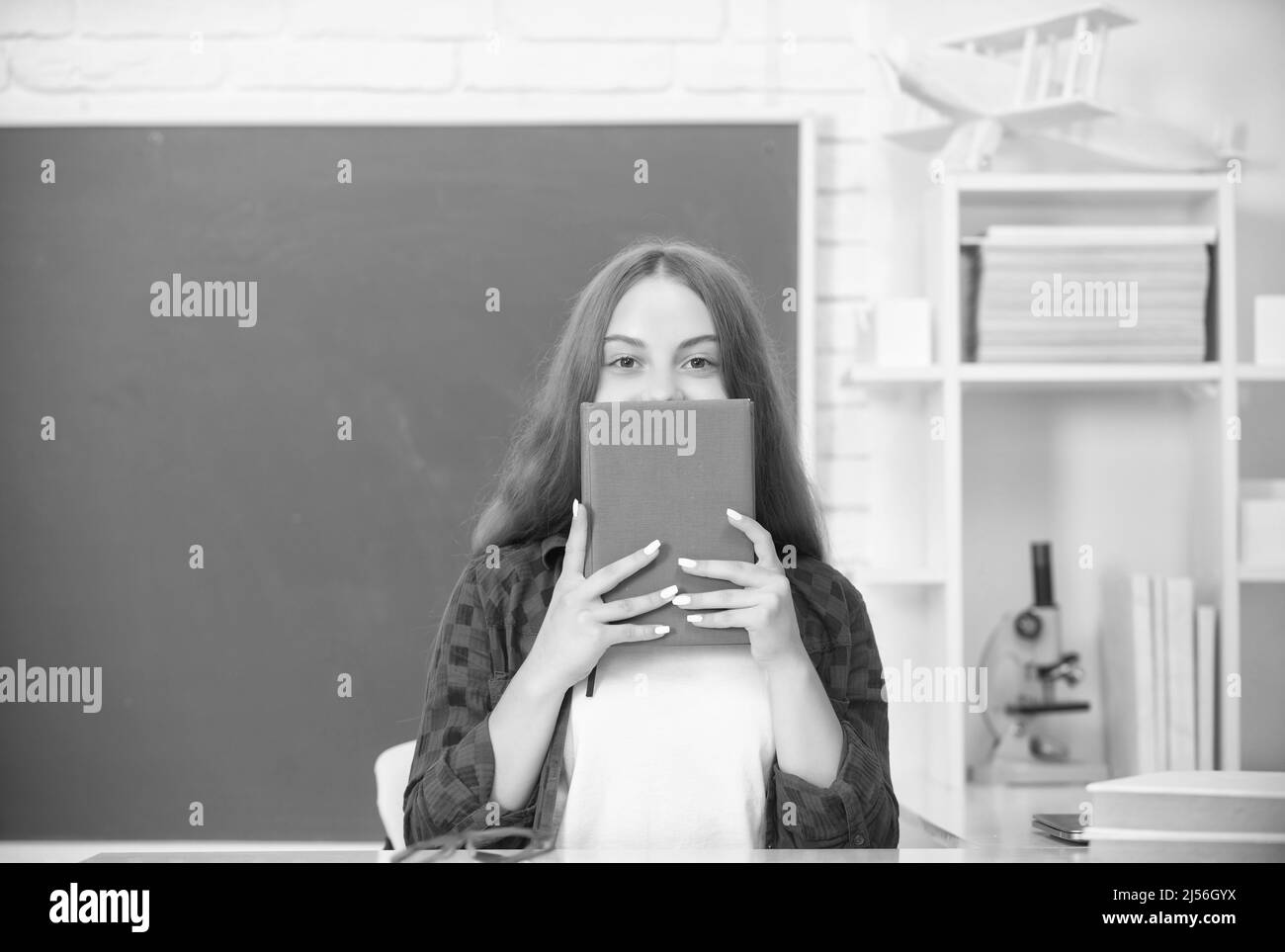 child hiding behind book at school on blackboard background, knowledge ...