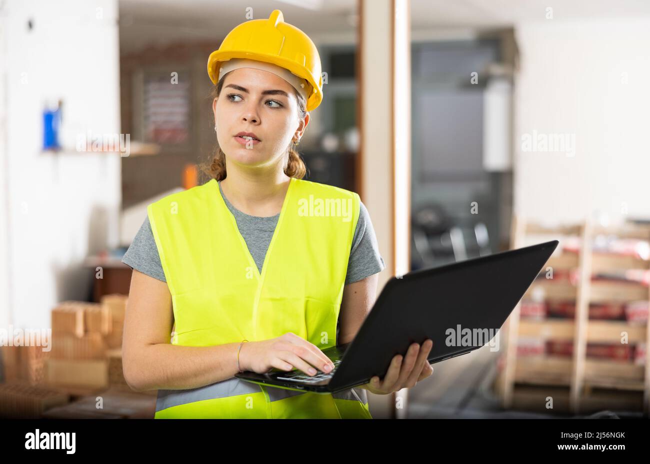 Female contractor using laptop to check plan of building under ...