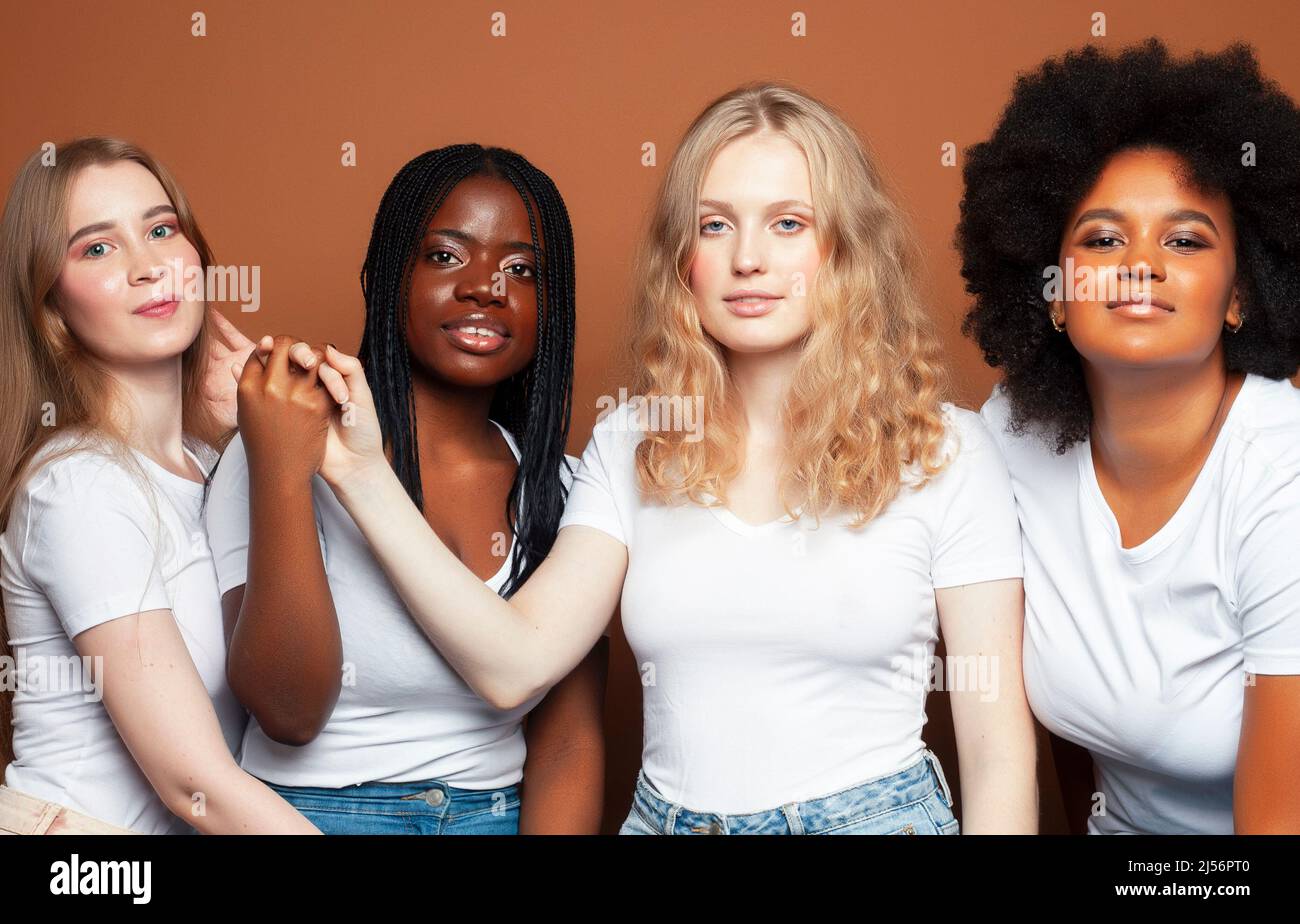 young pretty african and caucasian women posing cheerful together on brown background, lifestyle ...