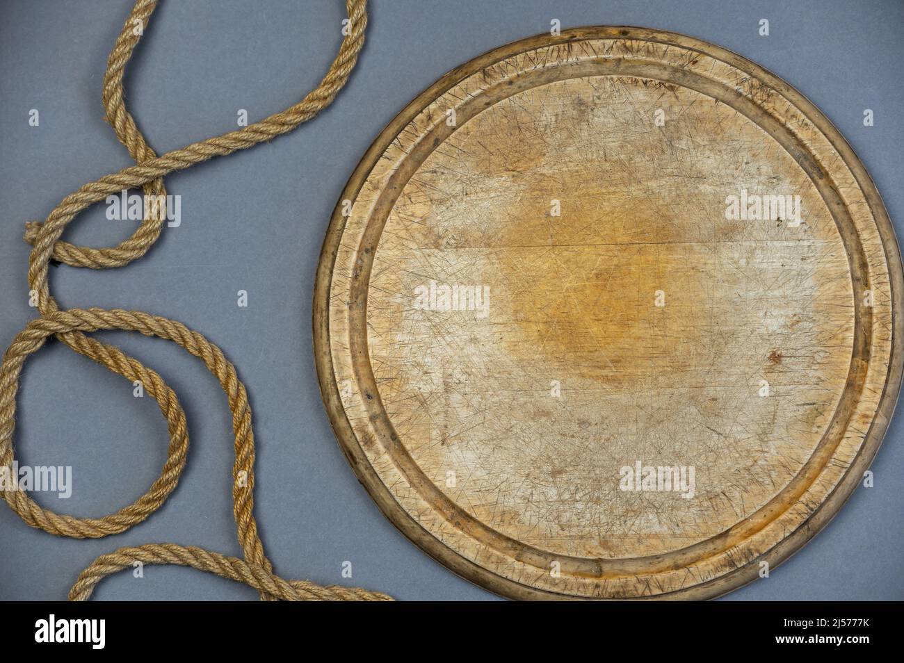 Round wooden cutting board and ship's rope against the gray background ...