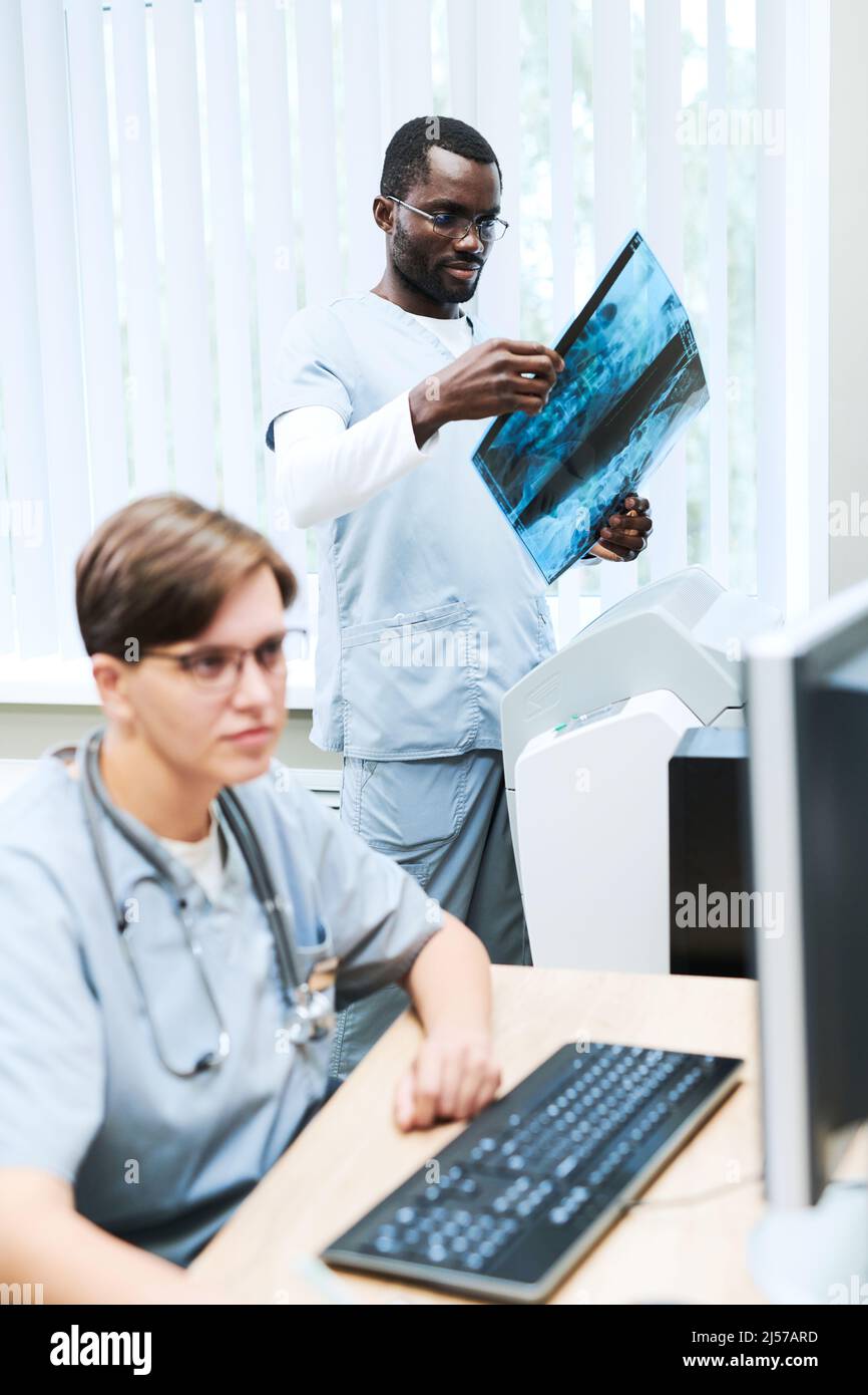 Serious African-American radiologist with stubble standing at printer ...