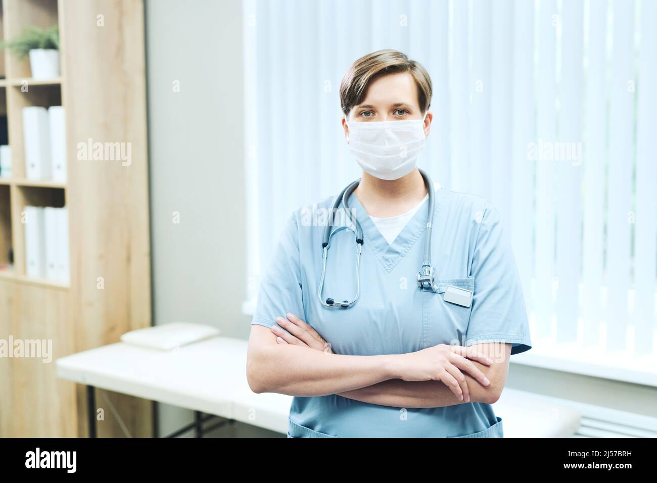 Portrait of fenale medical intern in facial mask standing with crossed ...