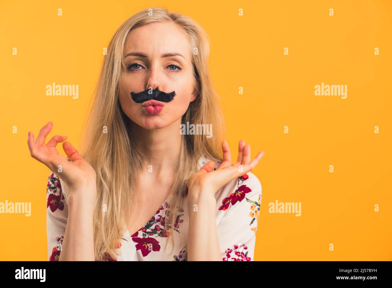 Portrait young blond Caucasian woman having fake mustache on her face, kissing gesture isolated ...