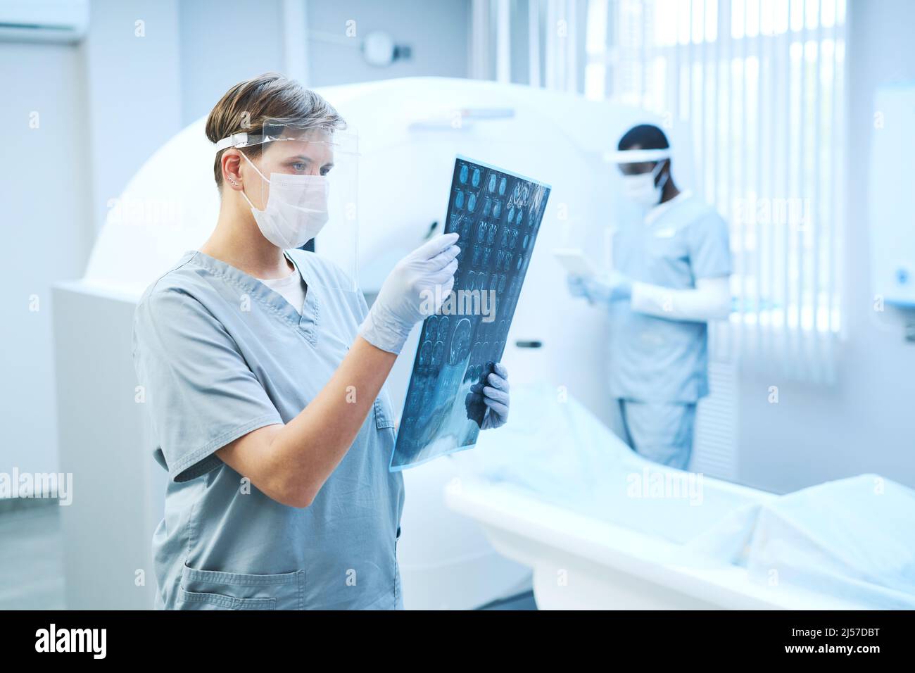 Focused radiologist in safety shield working with brain x-ray image ...