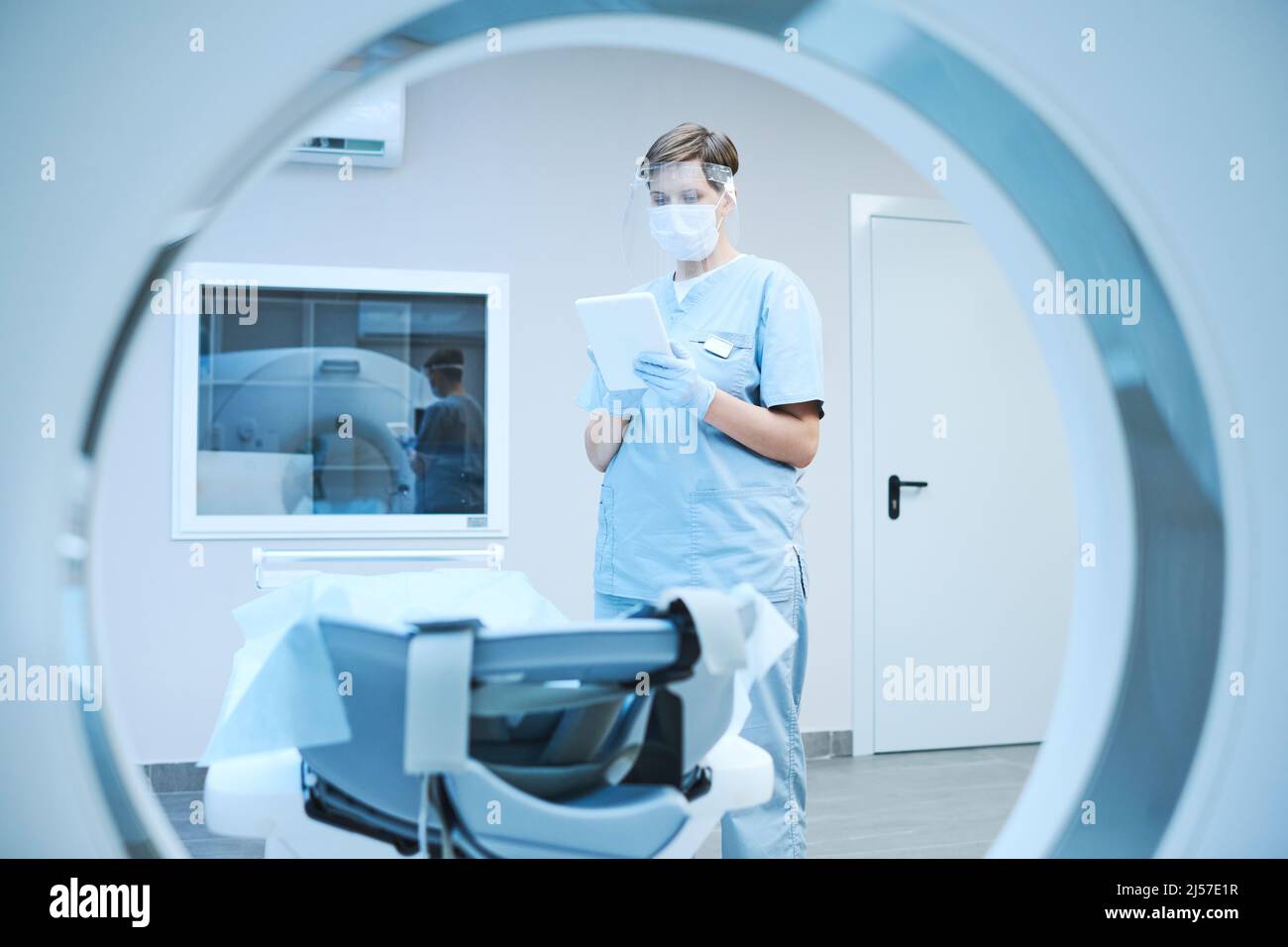 Serious nurse in protective mask and gloves using tablet and reading ...