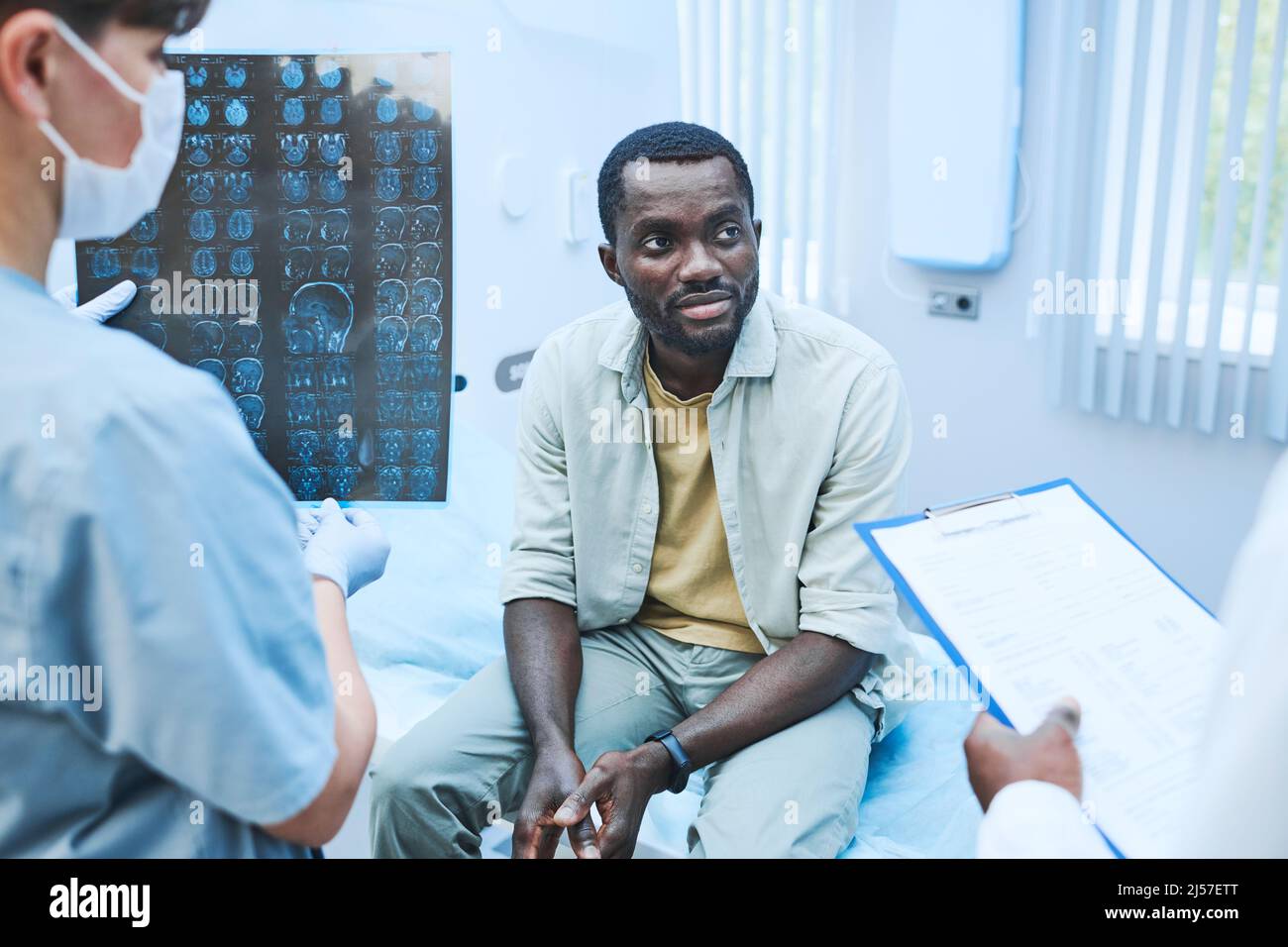 Confused Black patient with beard sitting on examination table and ...