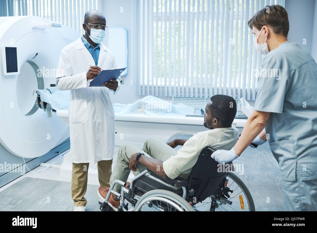 Afro-American doctor in mask with clipboard commenting MRI result to ...