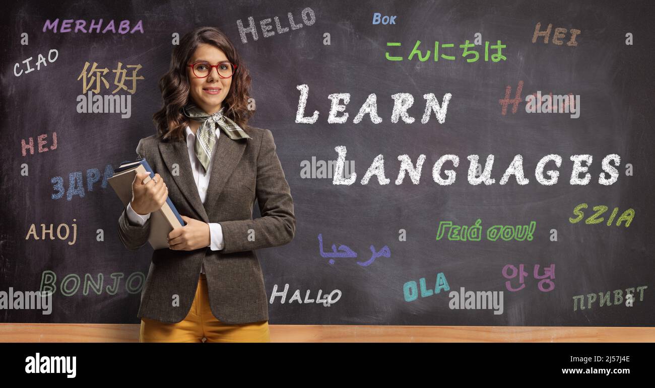 Young female language teacher holding books and posing in front of a ...