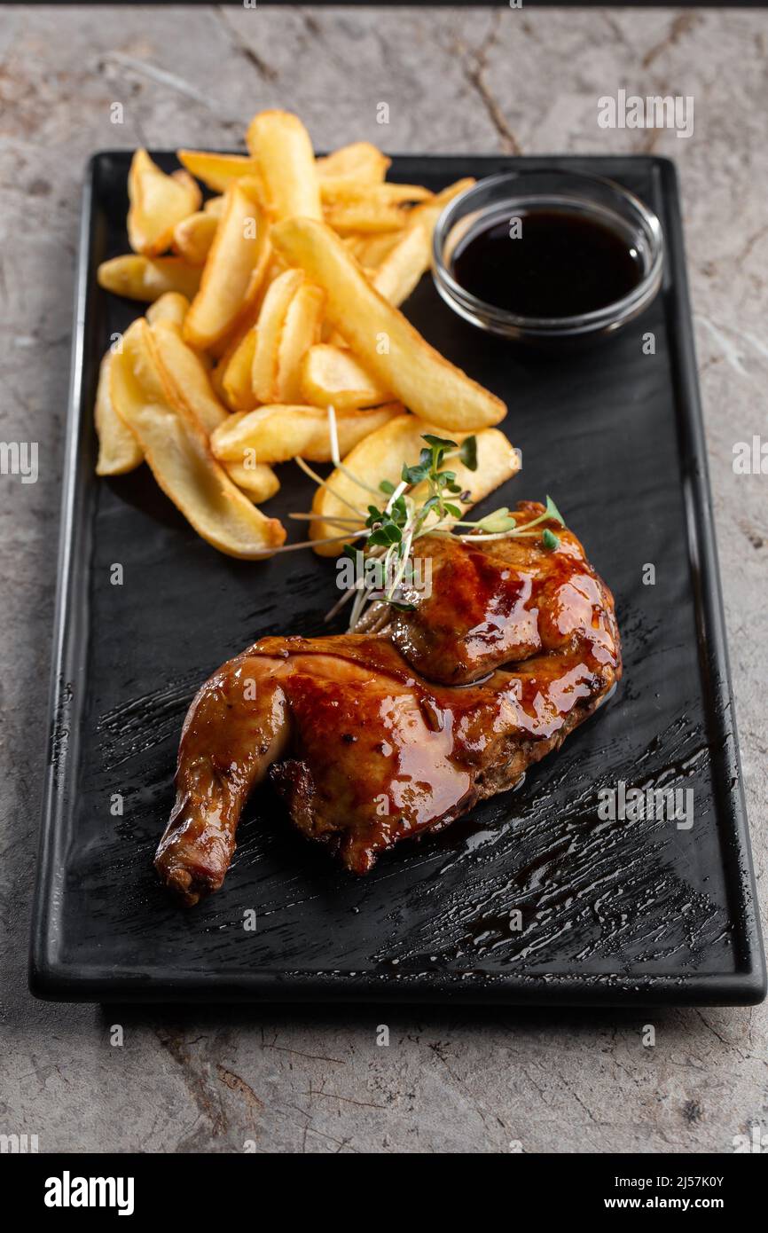 Grilled quail carcass with french fries on plate over black stone ...