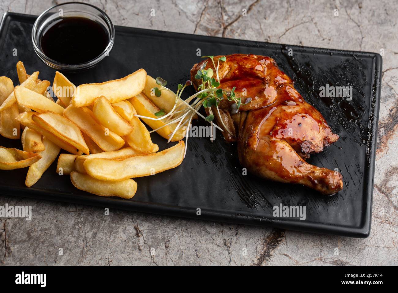 Grilled quail carcass with french fries on plate over black stone ...