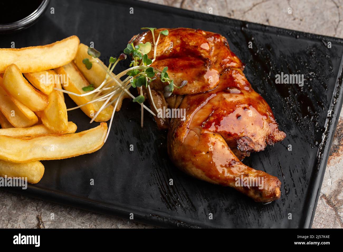 Grilled quail carcass with french fries on plate over black stone ...