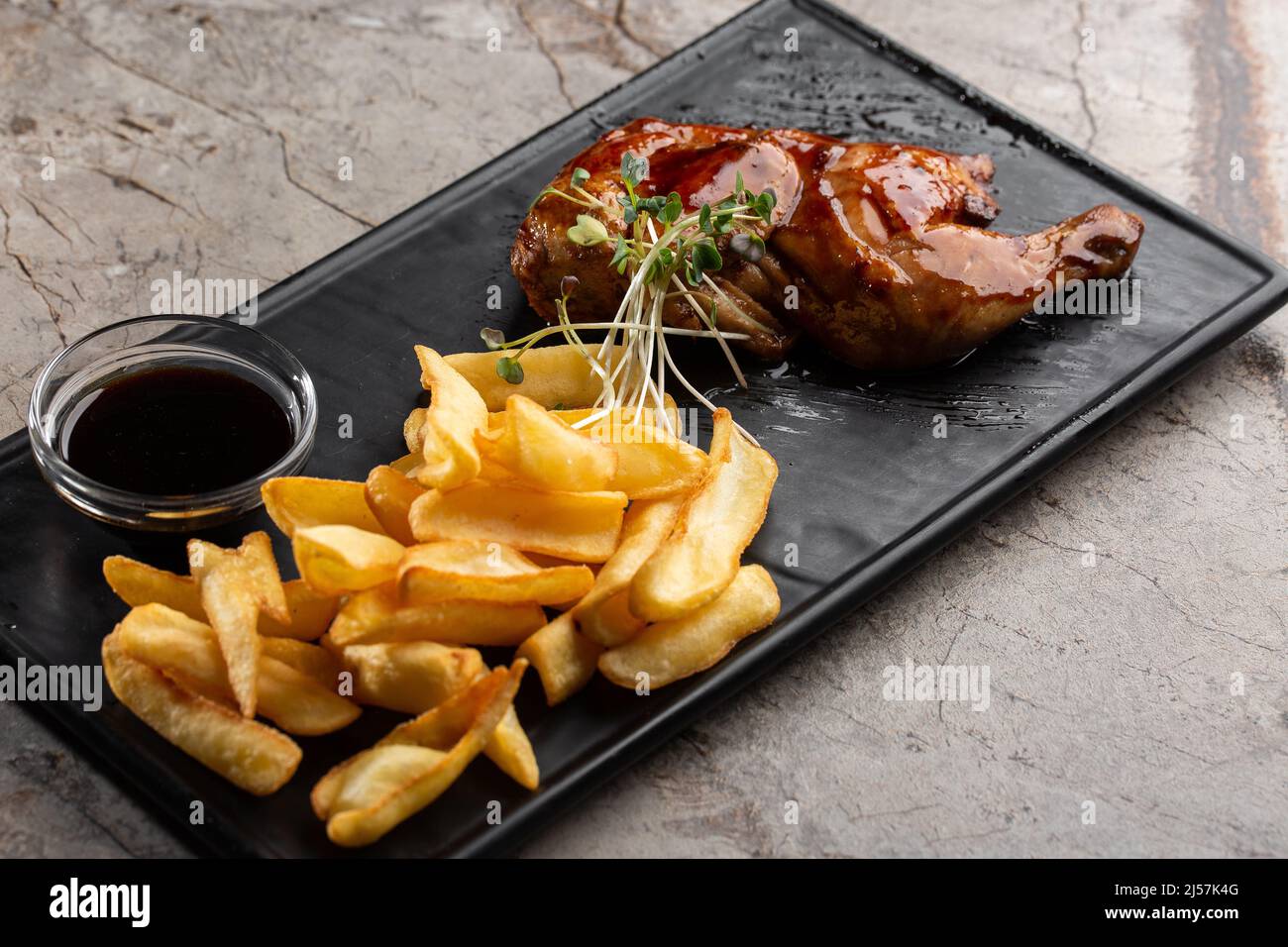 Grilled quail carcass with french fries on plate over black stone ...
