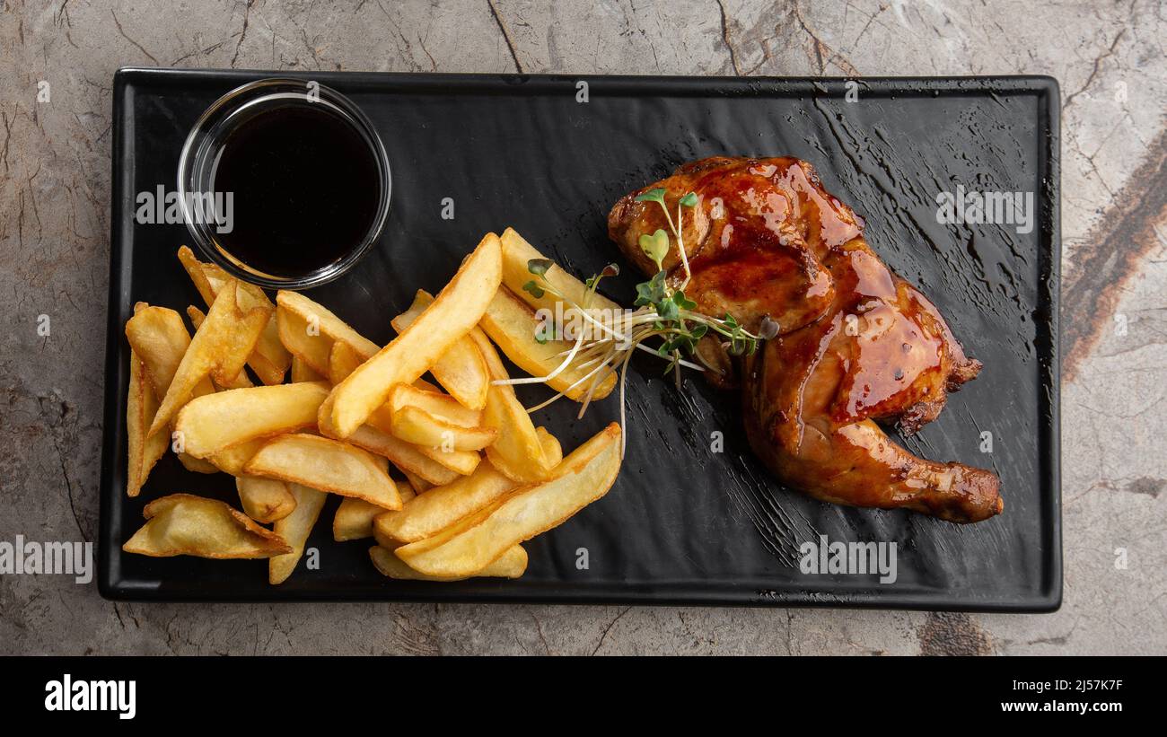 Grilled quail carcass with french fries on plate over black stone ...