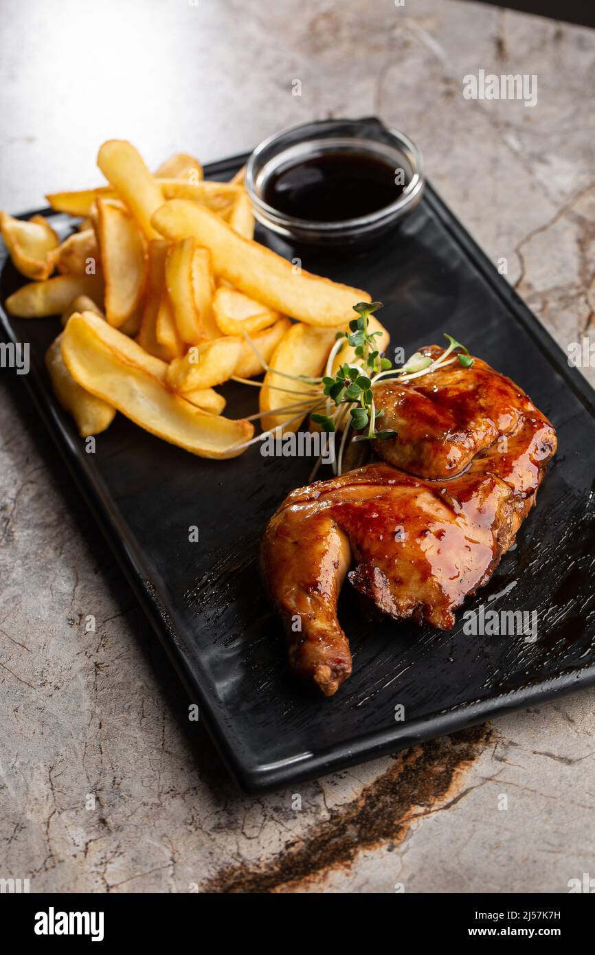 Grilled quail carcass with french fries on plate over black stone ...