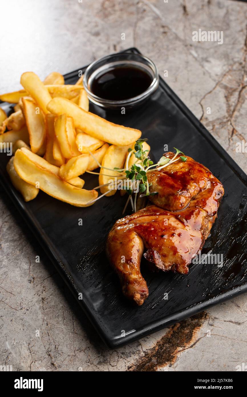 Grilled quail carcass with french fries on plate over black stone ...