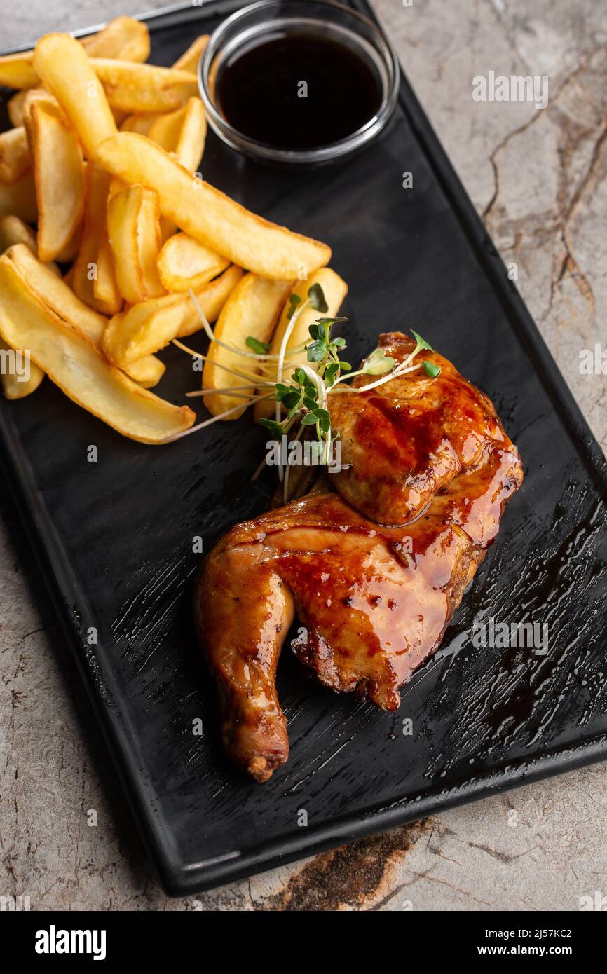 Grilled quail carcass with french fries on plate over black stone ...