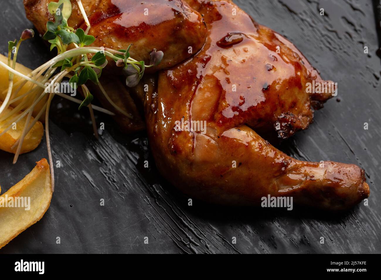 Grilled quail carcass with french fries on plate over black stone ...