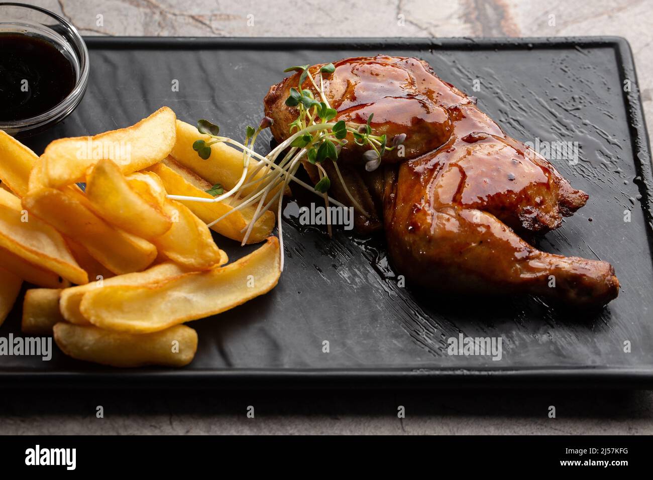 Grilled quail carcass with french fries on plate over black stone ...