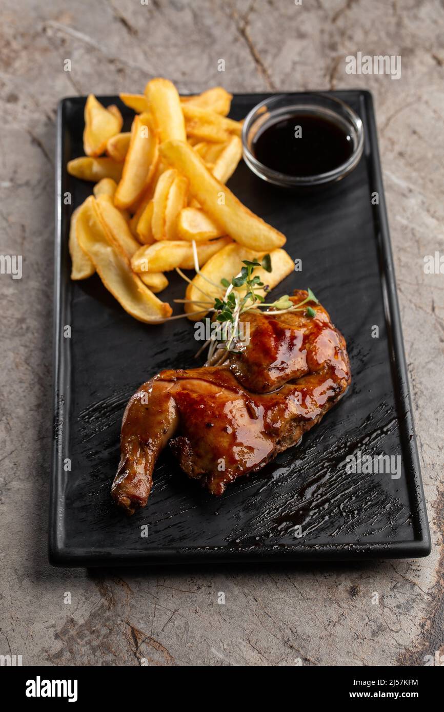Grilled quail carcass with french fries on plate over black stone ...
