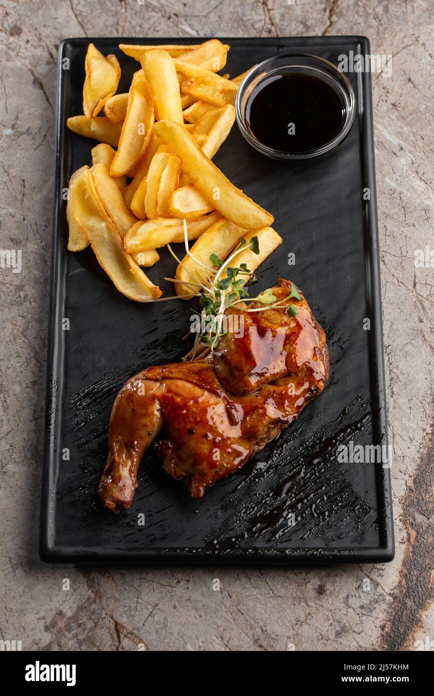 Grilled quail carcass with french fries on plate over black stone ...