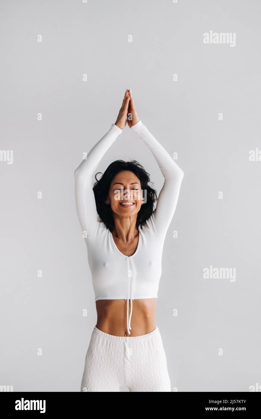 a female yogi in white clothes with her hands up meditates in the Yoga ...