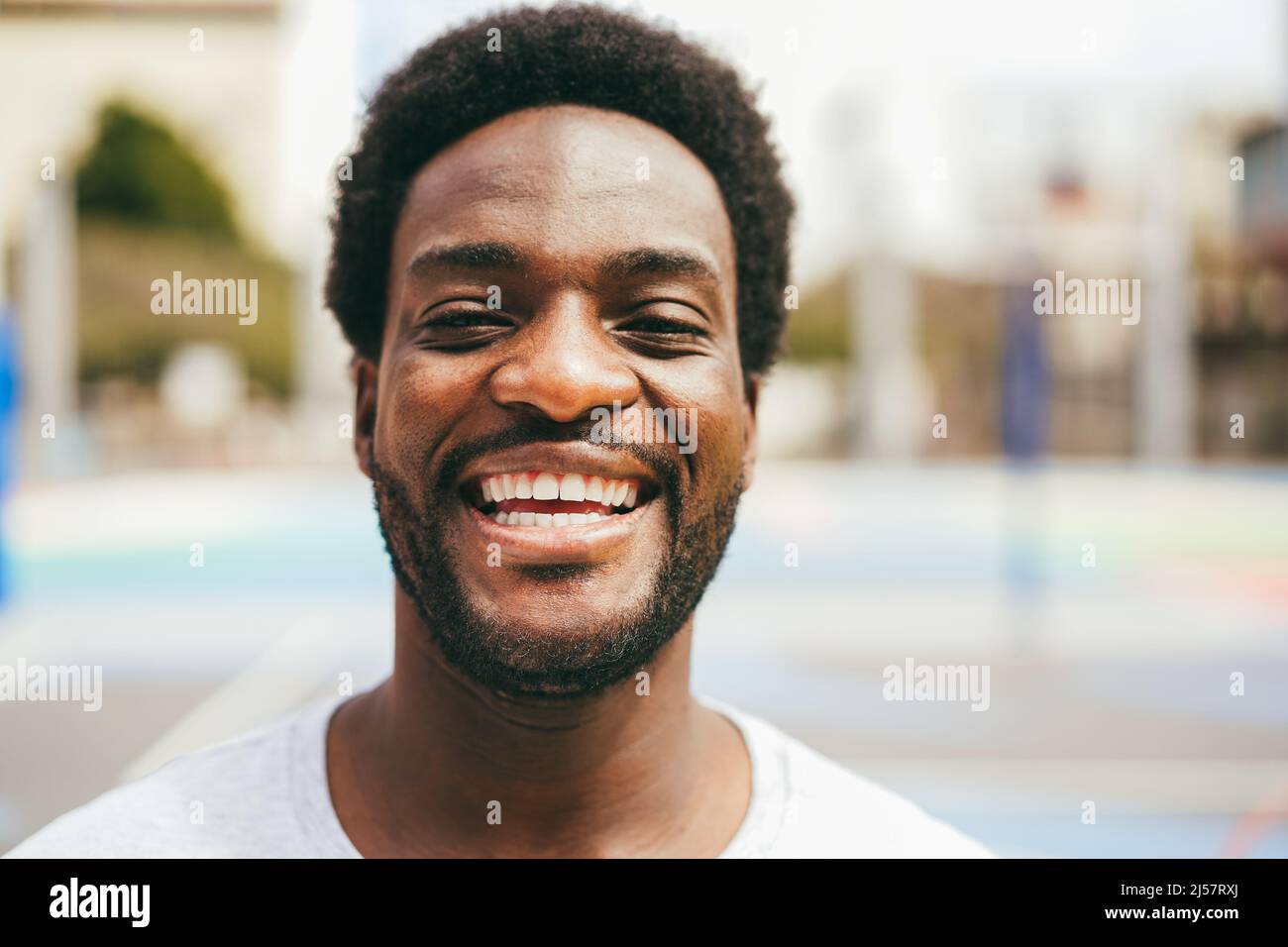 Happy African man smiling at camera inside basketball court - Focus on ...